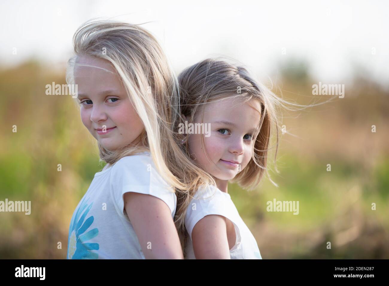 Two little girls stand with their backs to each other in the field ...