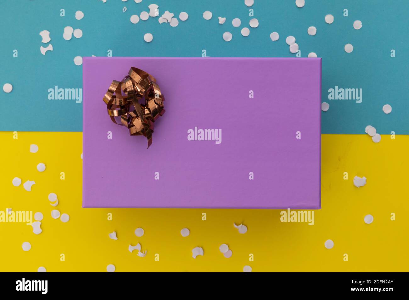 Purple gift box with ribbon and white confetti on yellow and blue ...