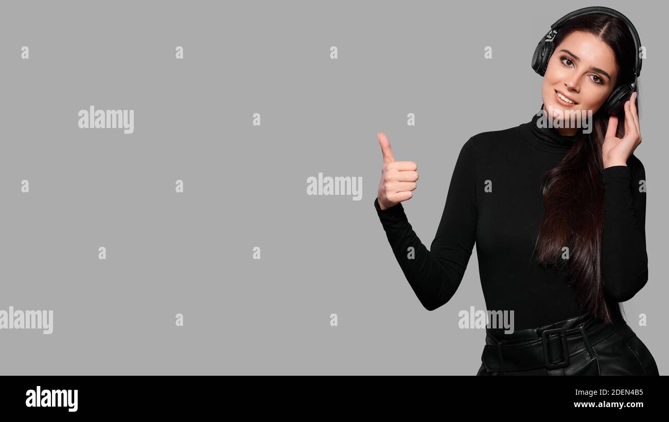 Smiling young woman in wireless headphones shows thumb up gesture ...