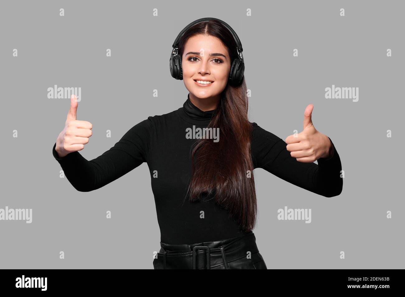 Smiling young woman in wireless headphones shows thumb up gesture ...