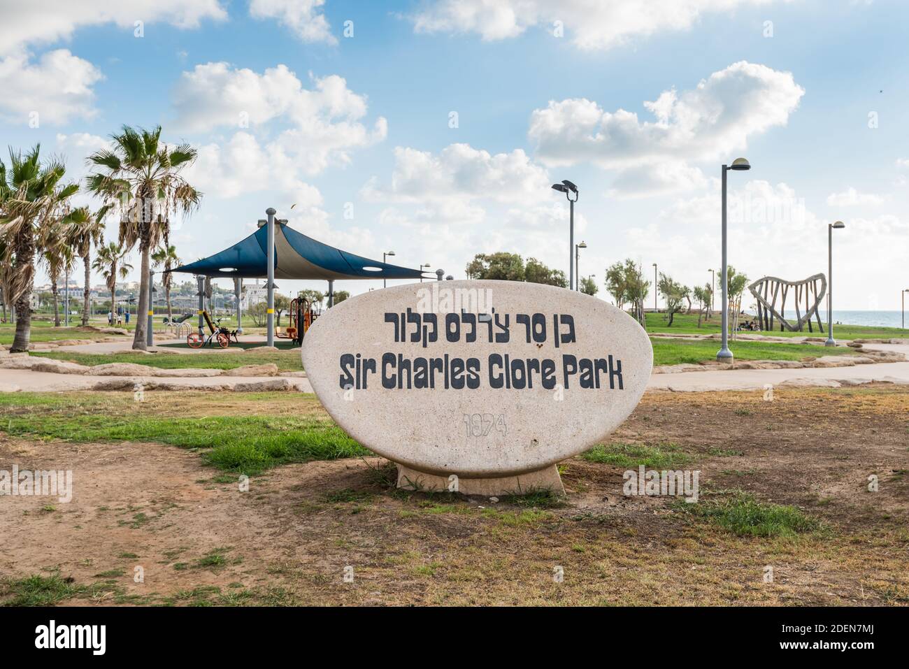 A stone with description Sir Charles Clore park and palm trees at the ...