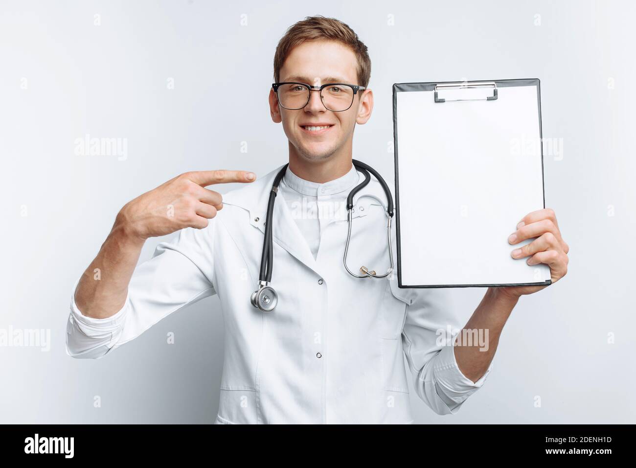 A young doctor shows a folder with a blank sheet on the camera, on a ...