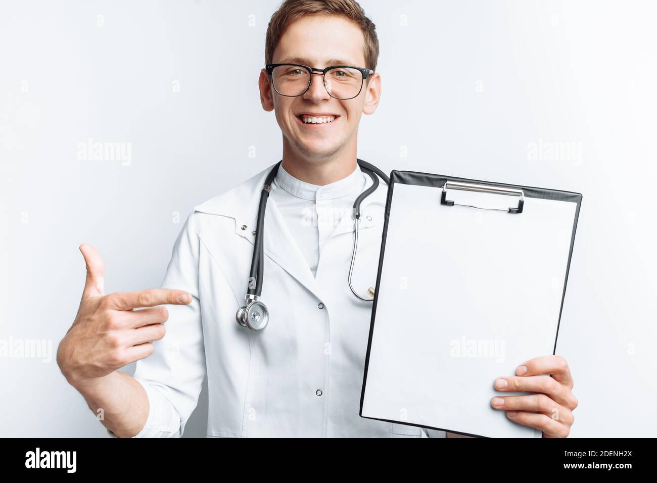 A young doctor shows a folder with a blank sheet on the camera, on a ...
