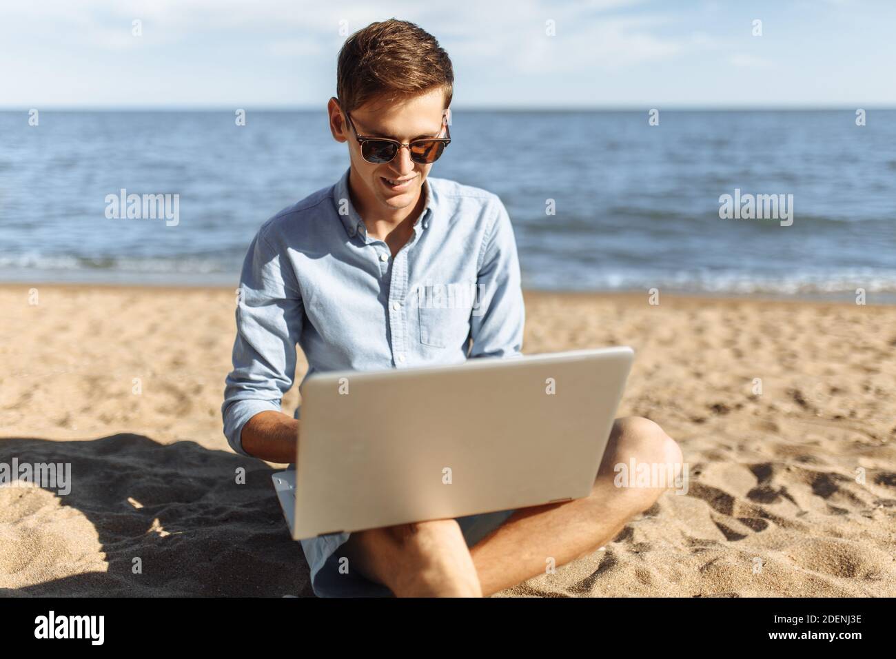 Young guy with glasses, working on his laptop on the beach, work on ...