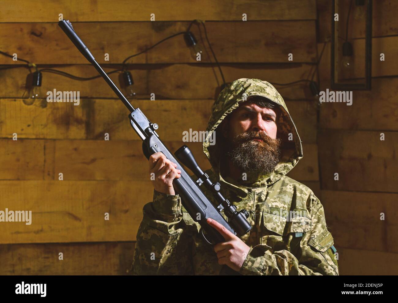 Man with beard wears camouflage hooded clothing, wooden interior ...