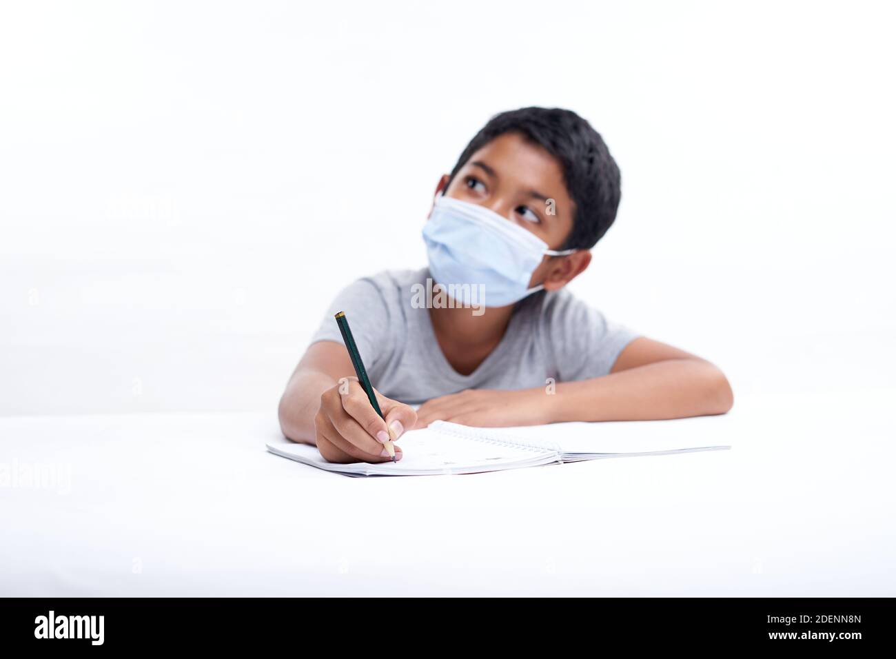 Schoolboy with a protective face mask writing in notebook at home ...