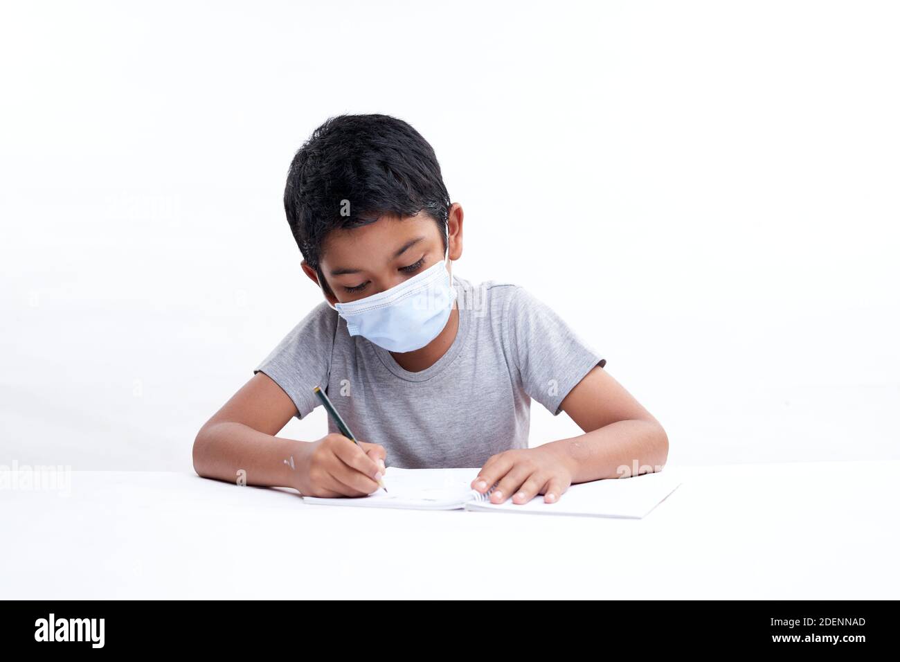 Schoolboy with a protective face mask writing in notebook at home ...