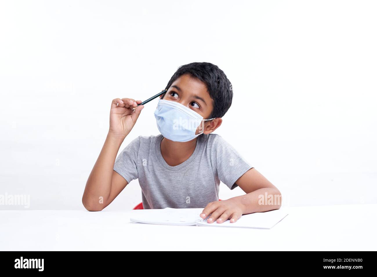 Schoolboy with a protective face mask writing in notebook at home ...