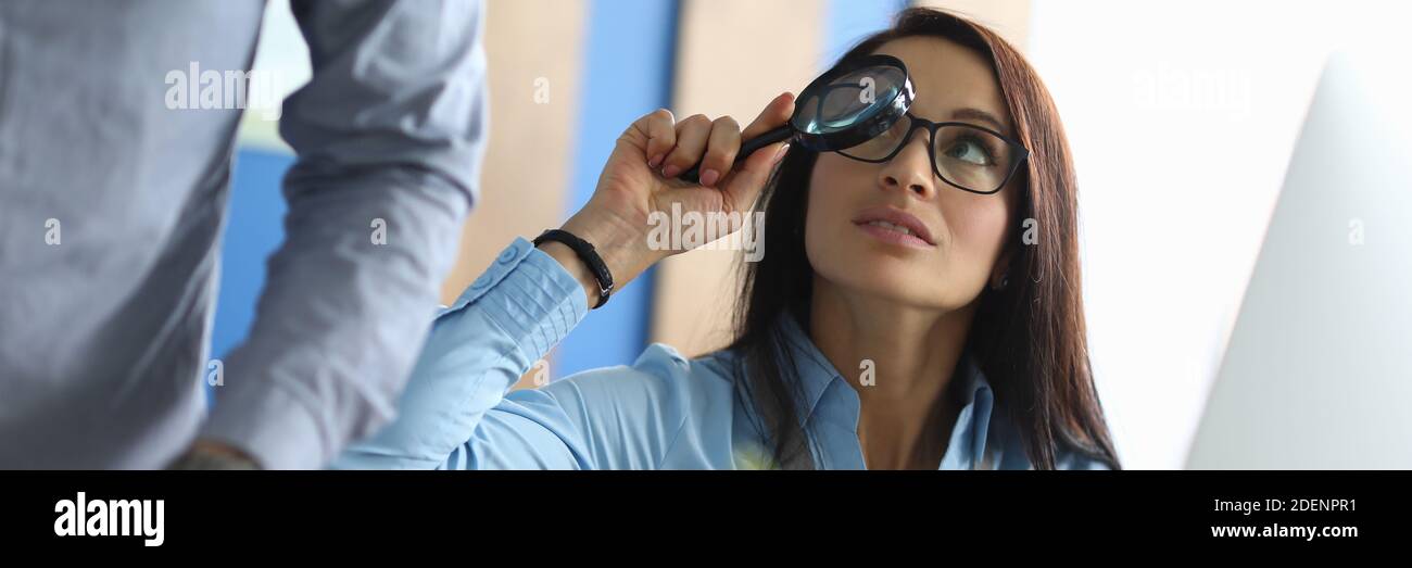 Woman sits at work desk and looks through magnifying glass at an ...