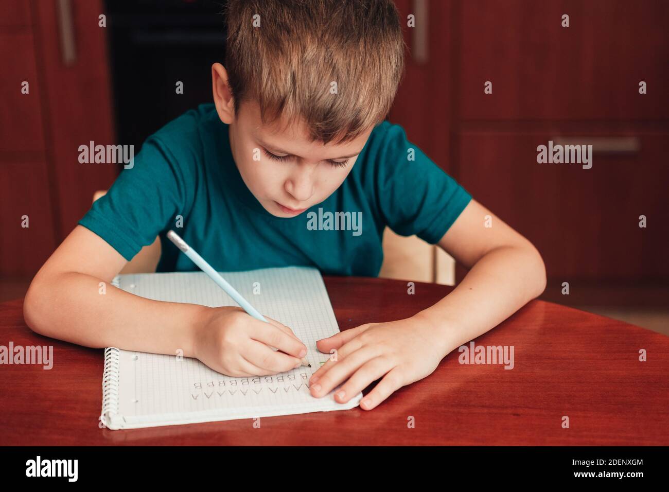 7 years old child writing letters in notebook sitting by table in ...