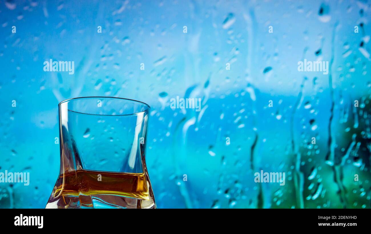 Whiskey in a glass against the background of a rainy window, drops on ...