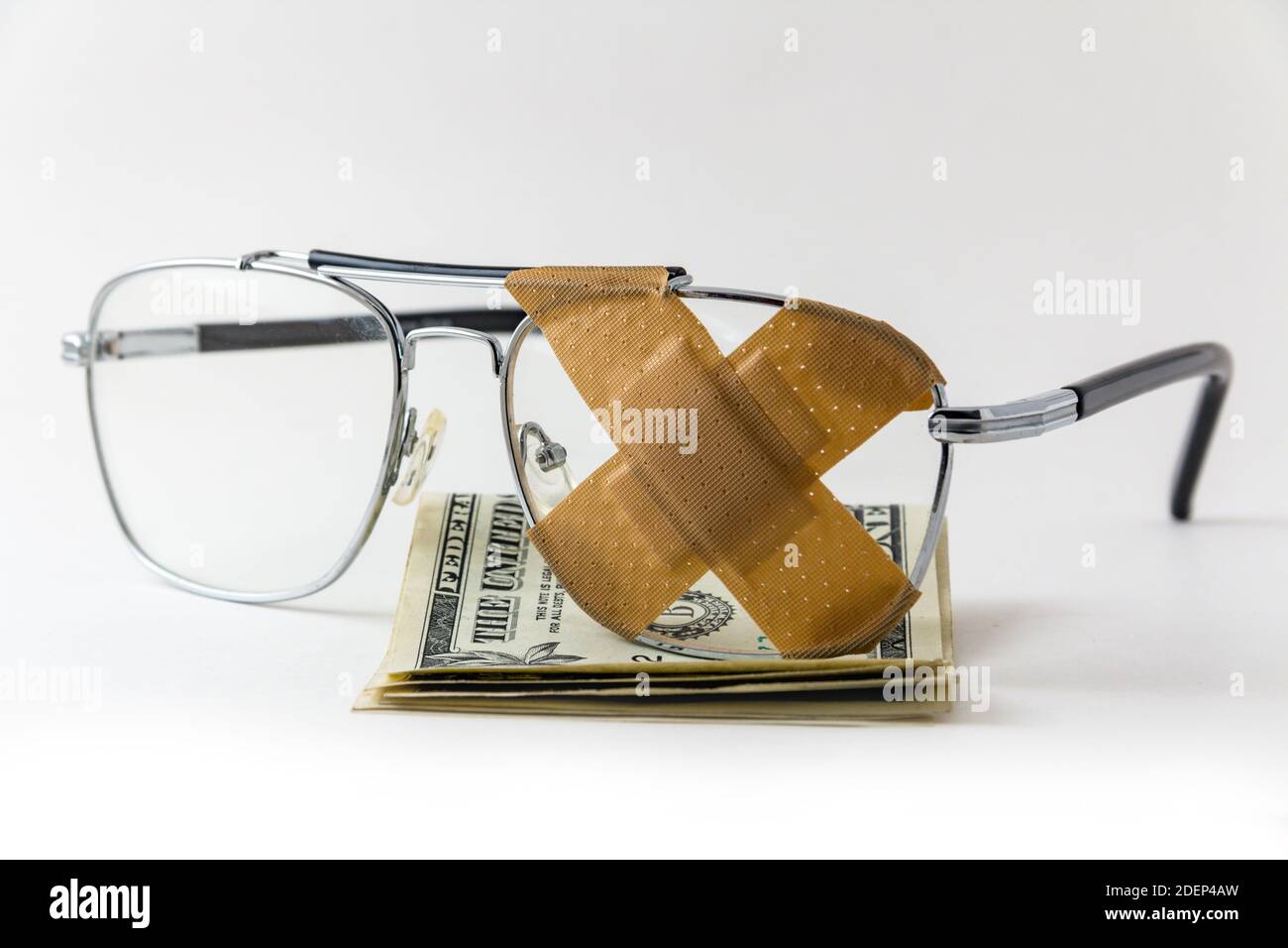 Eye glasses with band-aid X and dollar bills - healthcare is expensive ...