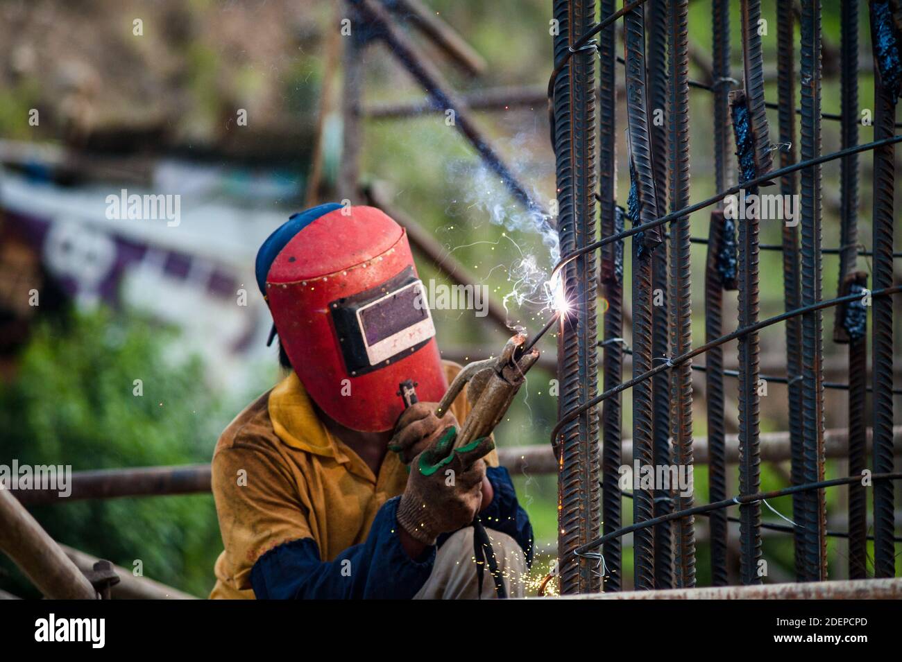 Welder in a red welding mask welding rebars for reinforced concrete ...
