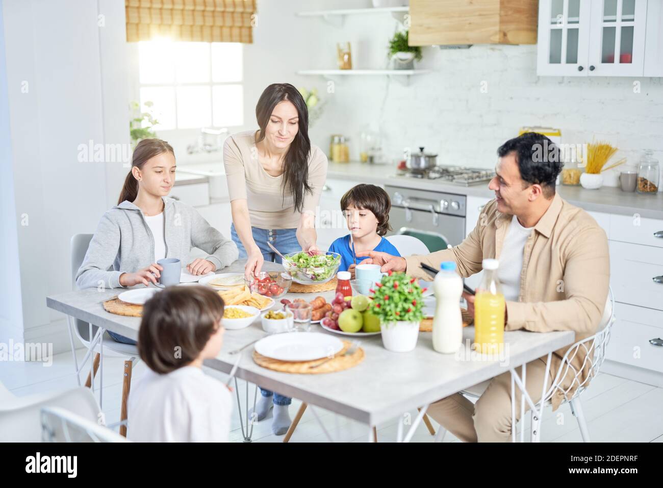 Caring hispanic woman serving salad for her husband and children ...