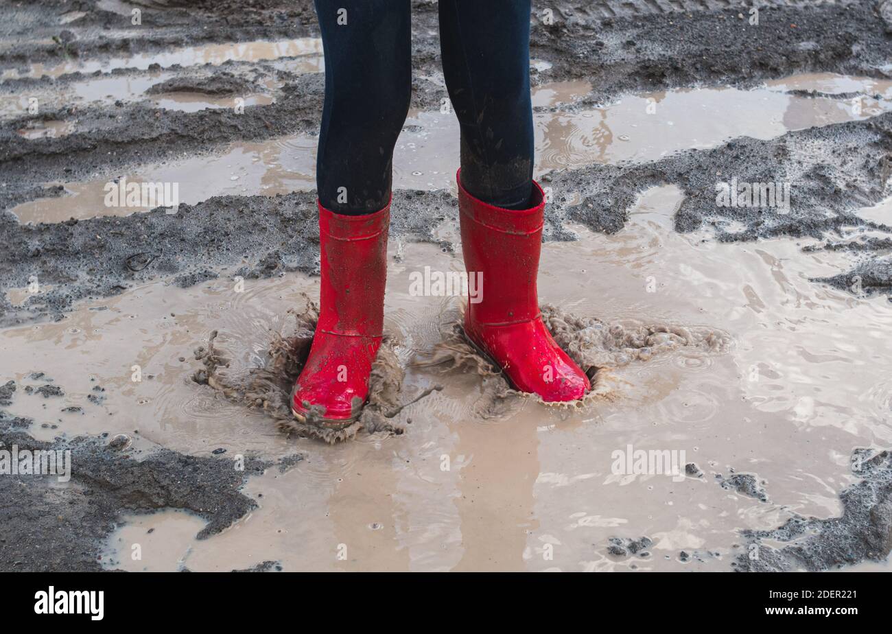 Legs of a girl jumping in a mud puddle, wearing red wellies, splashing ...
