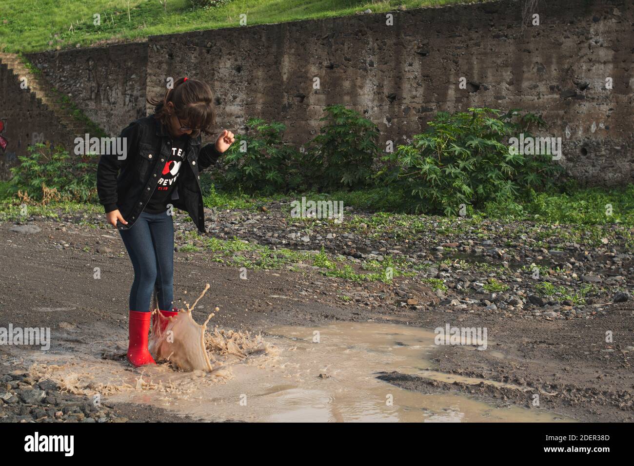 Girl jumping in muddy puddles wearing red wellies, filling up with mud ...