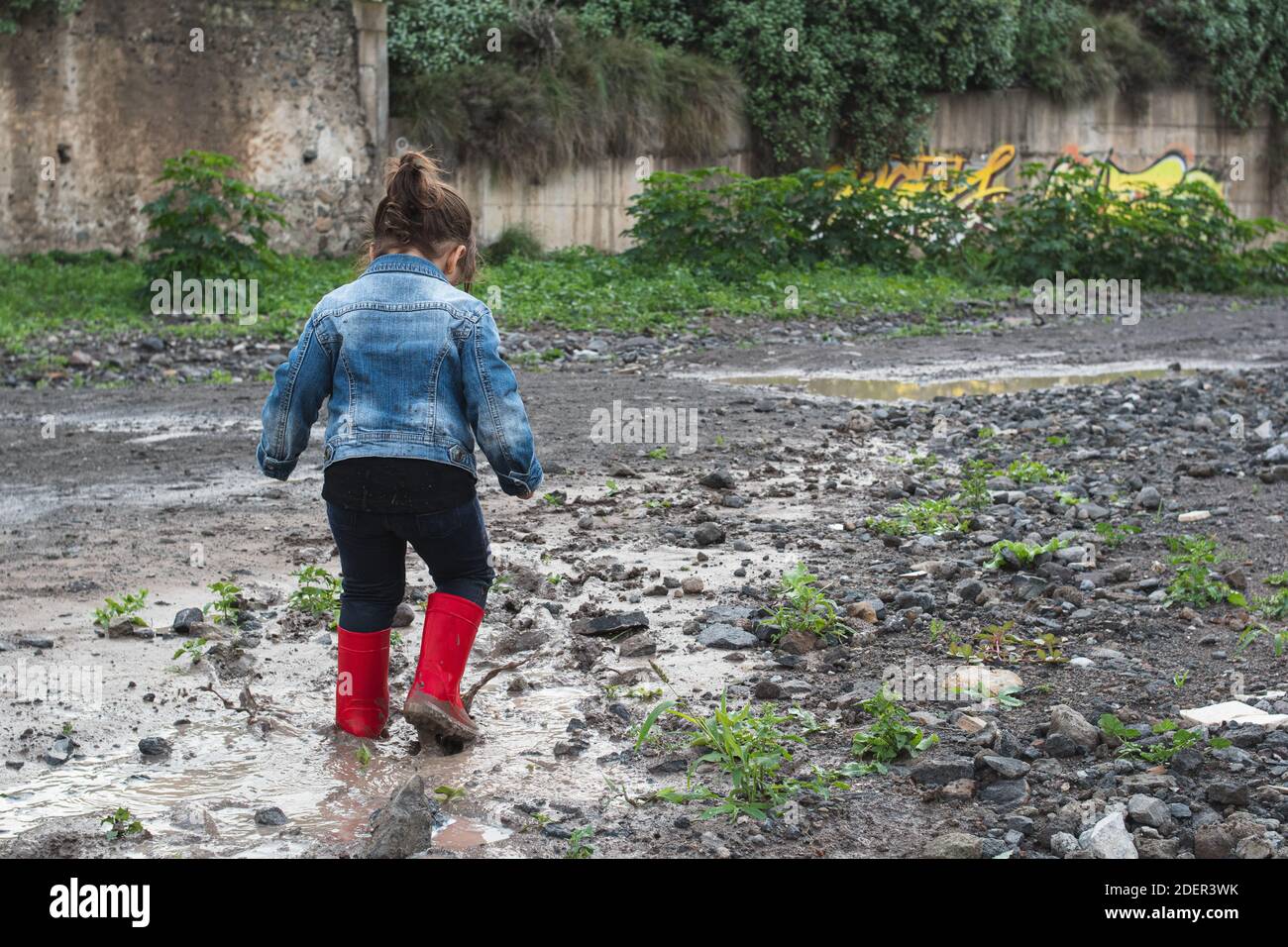 Girl jumping in muddy puddles wearing red wellies, filling up with mud ...