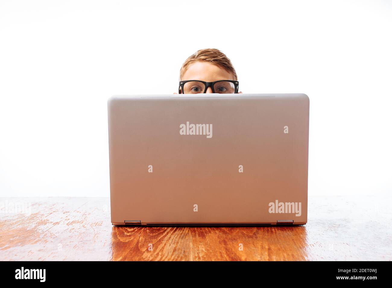 The face of a young man looks out from under the laptop, a teenager ...