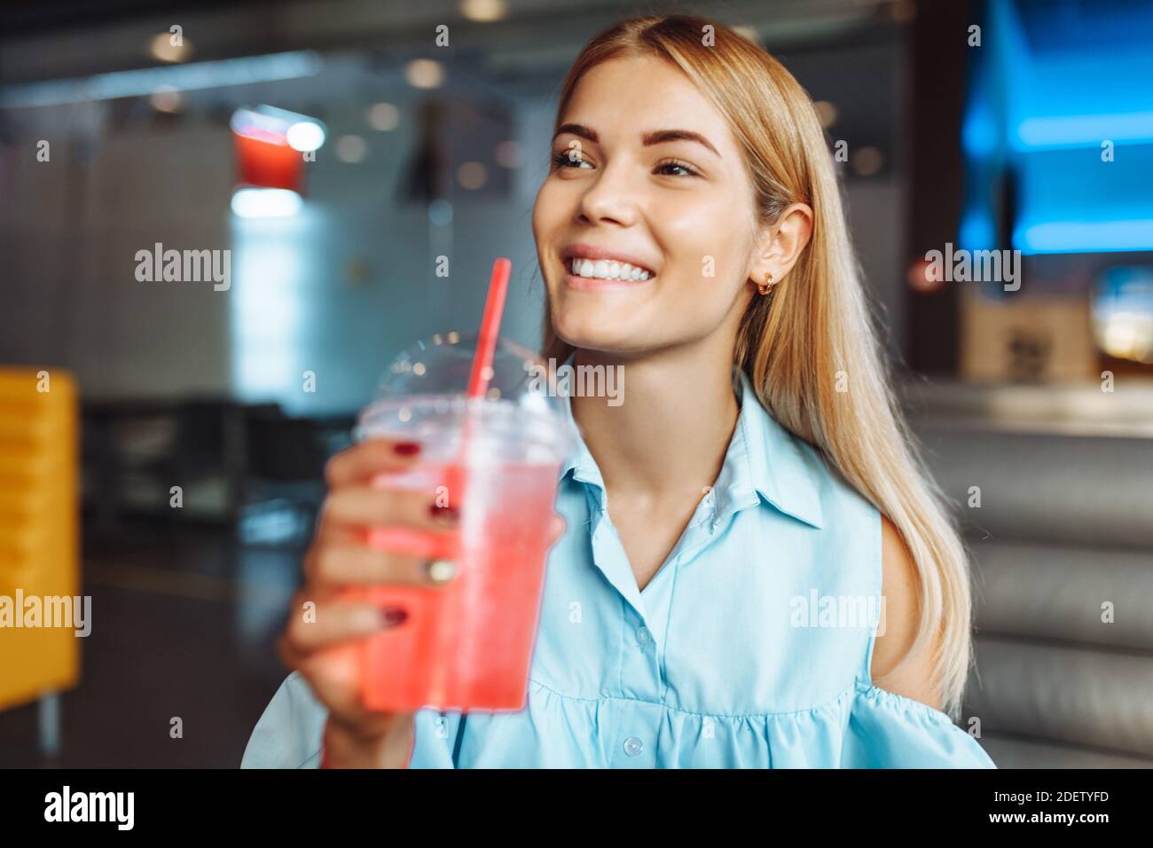Beautiful young cheerful girl, drinking a cocktail, sitting in a cafe ...