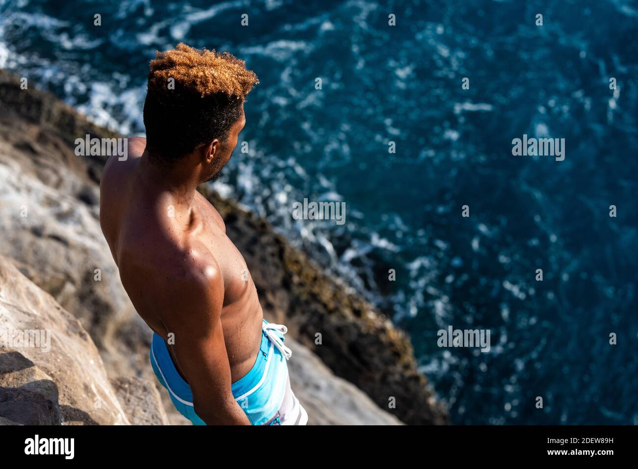 Male cliff diver looking at the ocean jump zone before diving in oahu ...