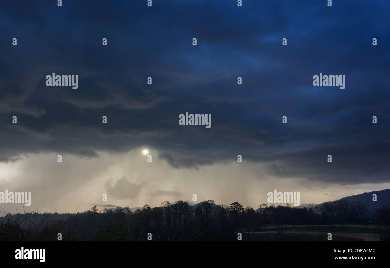 The sun as seen through a veil of rain at the edge of storm clouds ...