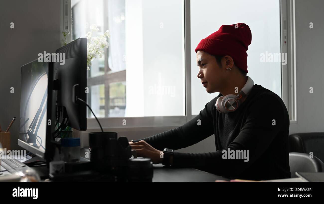 Side view of young photographer in red wool hat working with new ...
