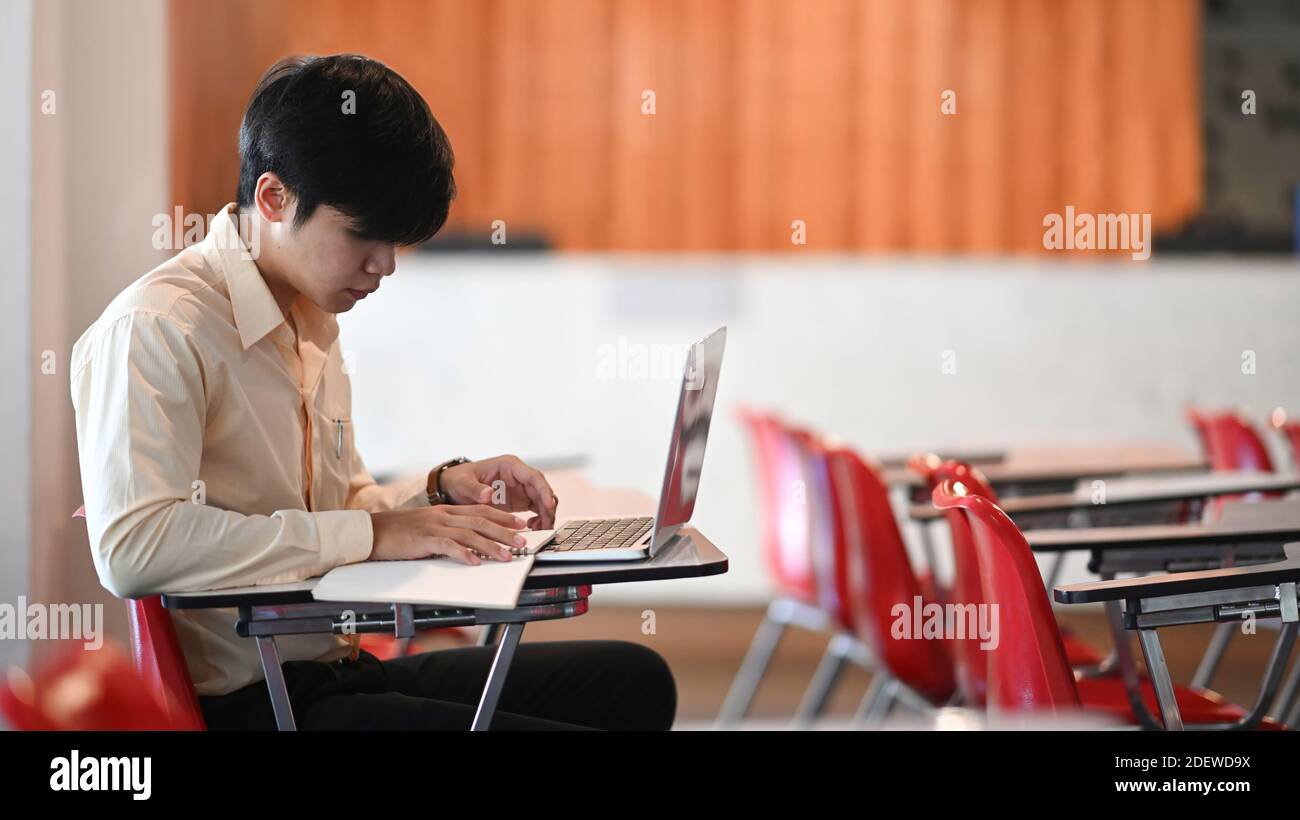 Side view of a young man college student using laptop on lecture chair ...