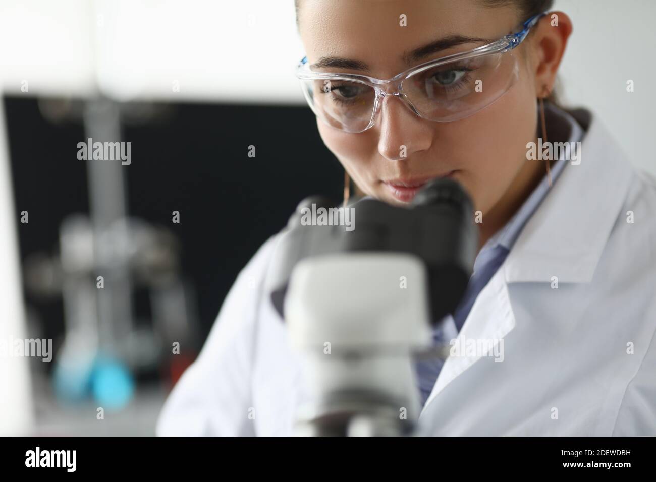 Chemist in goggles and white coat looks through microscope Stock Photo ...