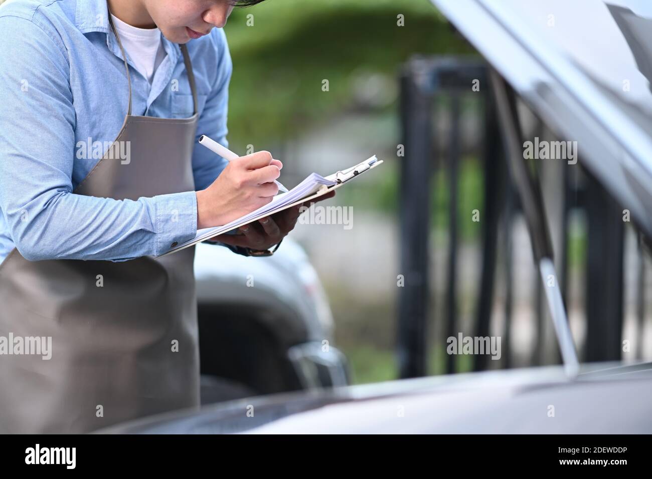 Automobile mechanic is checking a car engine and writing on the ...