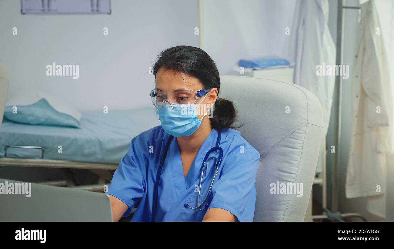 Ward assistant having protection mask and glasses writing a report on ...