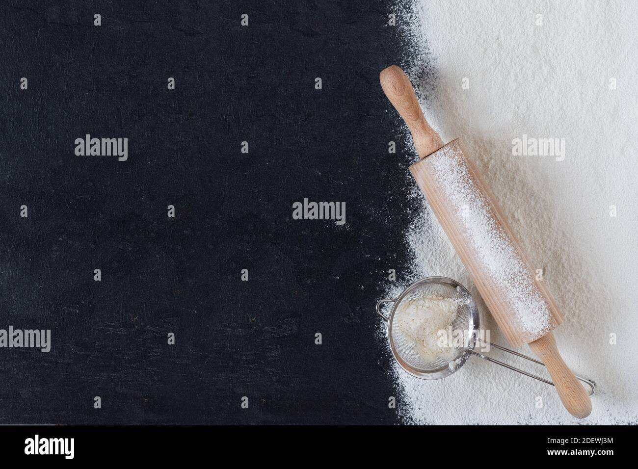 Sifted wheat flour over black surface with rolling pin and sieve top ...