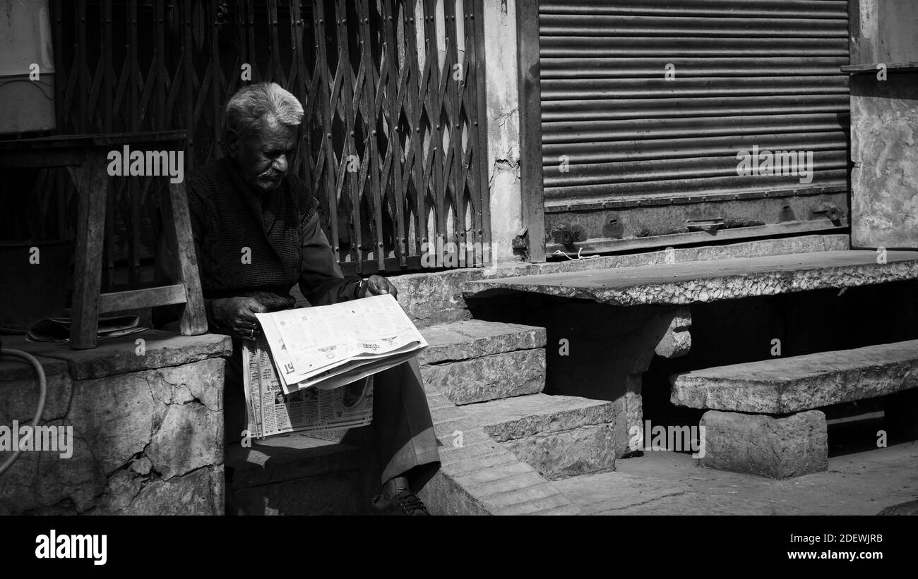 A man is sitting and reading a newspaper on a street corner in Bundi ...