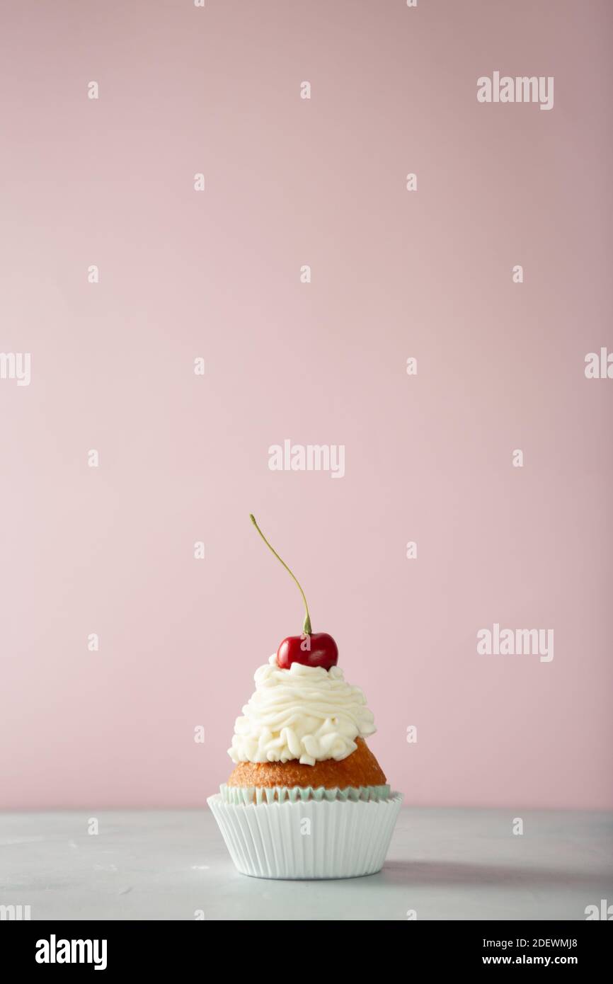 A vertical shot of a delicious cupcake with cream and cherry on top ...