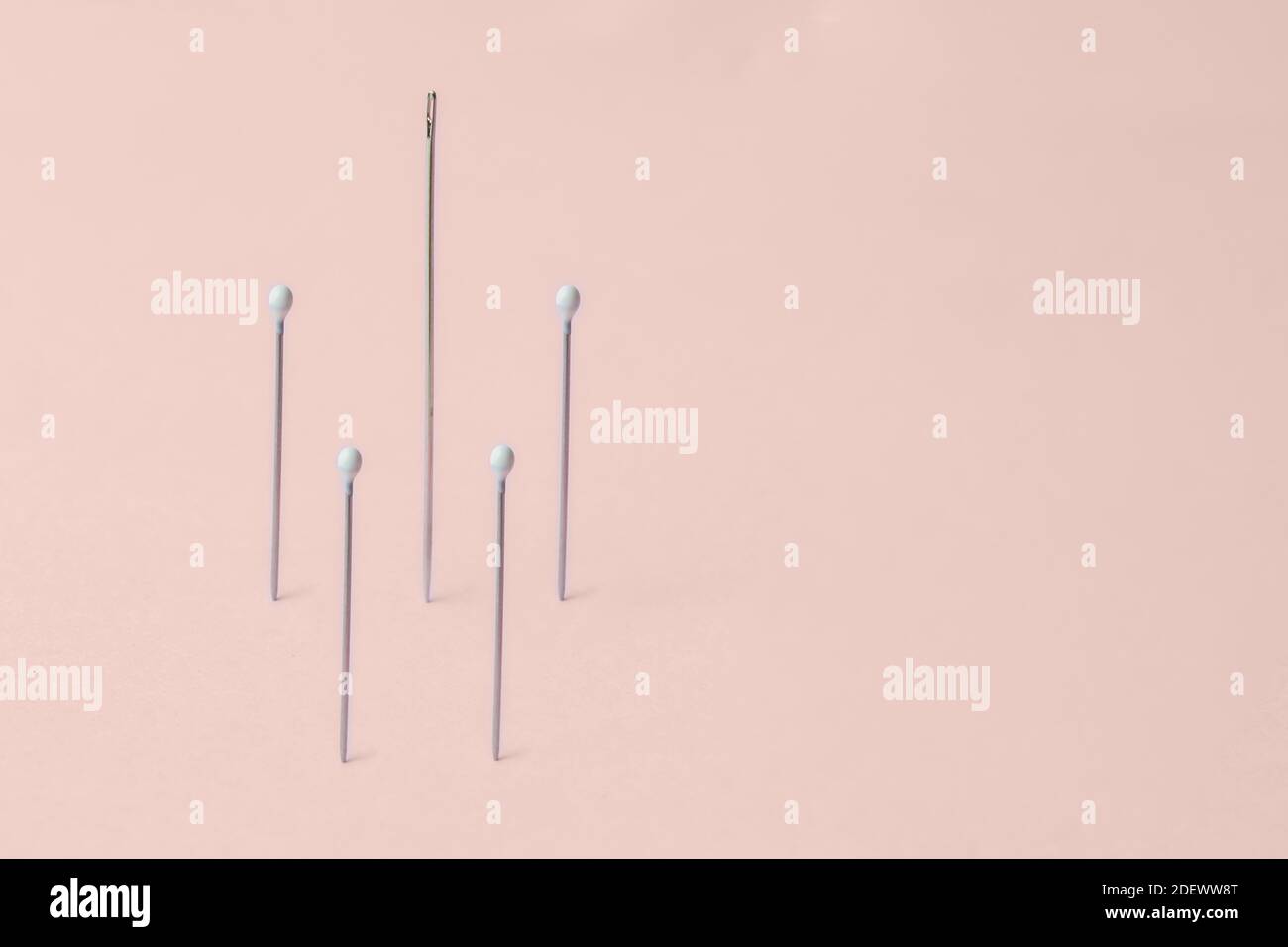 A needle for threading thread surrounded by pearl-headed pins on color ...