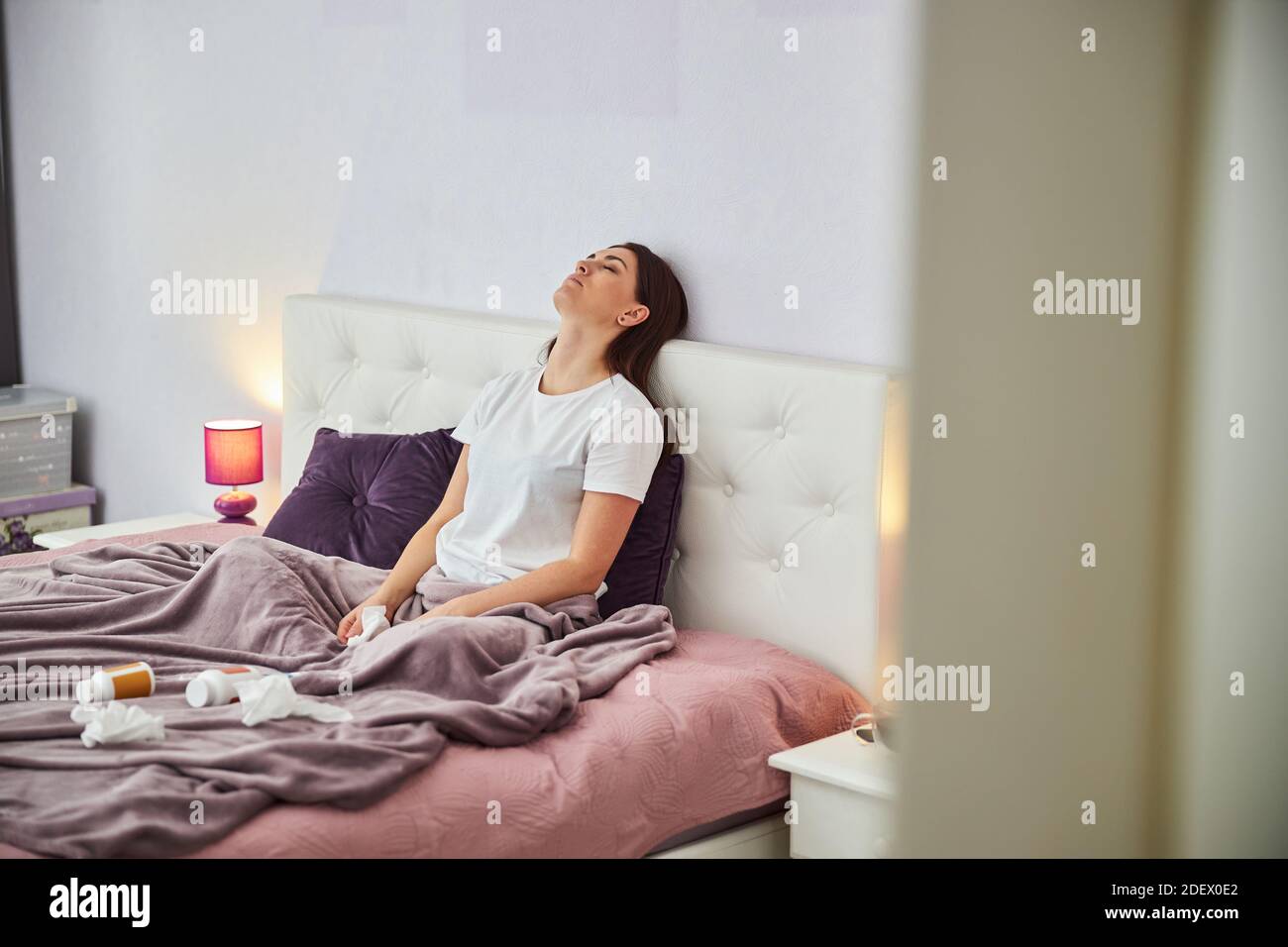 Tired woman leaning back on a headboard Stock Photo - Alamy