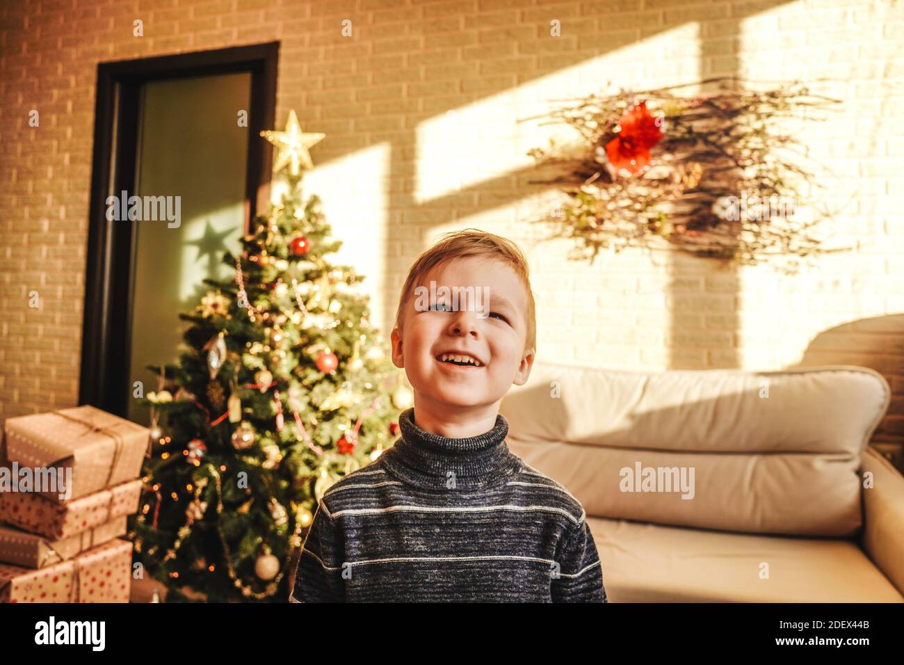 Little boy praying at Christmas Eve, Christmas tree and gift boxes on ...