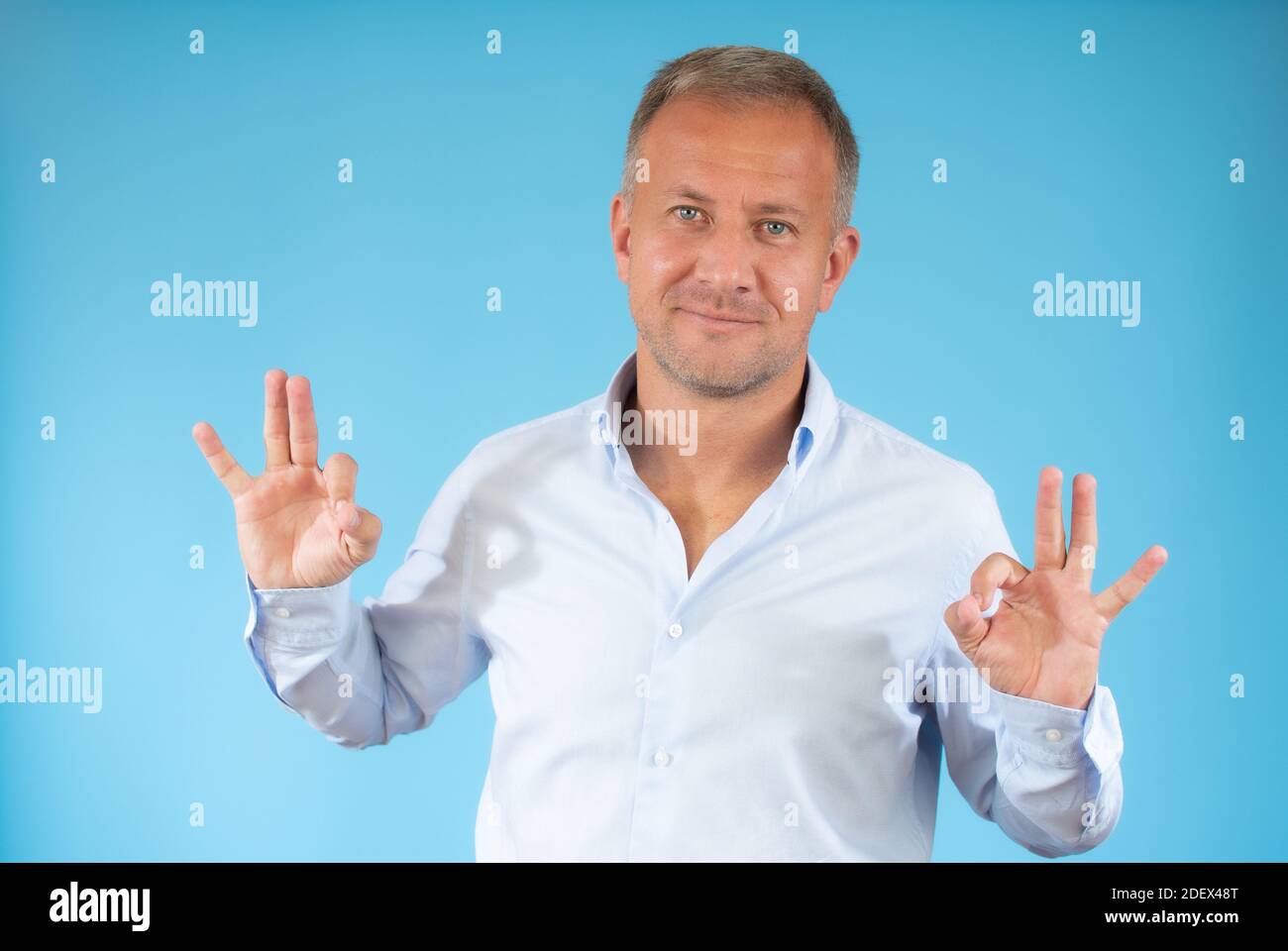Young handsome man with blue eyes smiling positive doing okay sign with ...