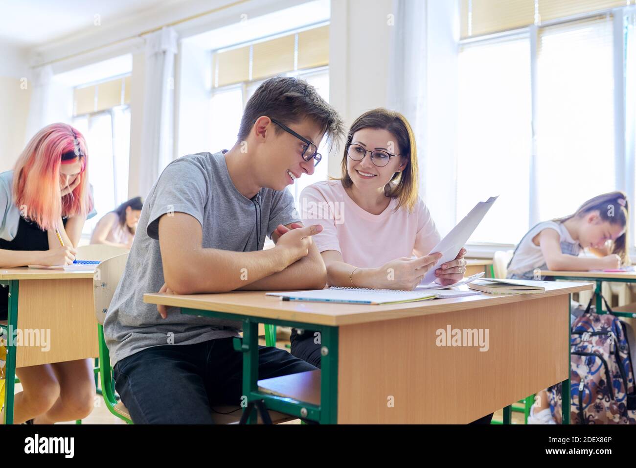 Lesson in class of high school students, female teacher sitting at desk ...