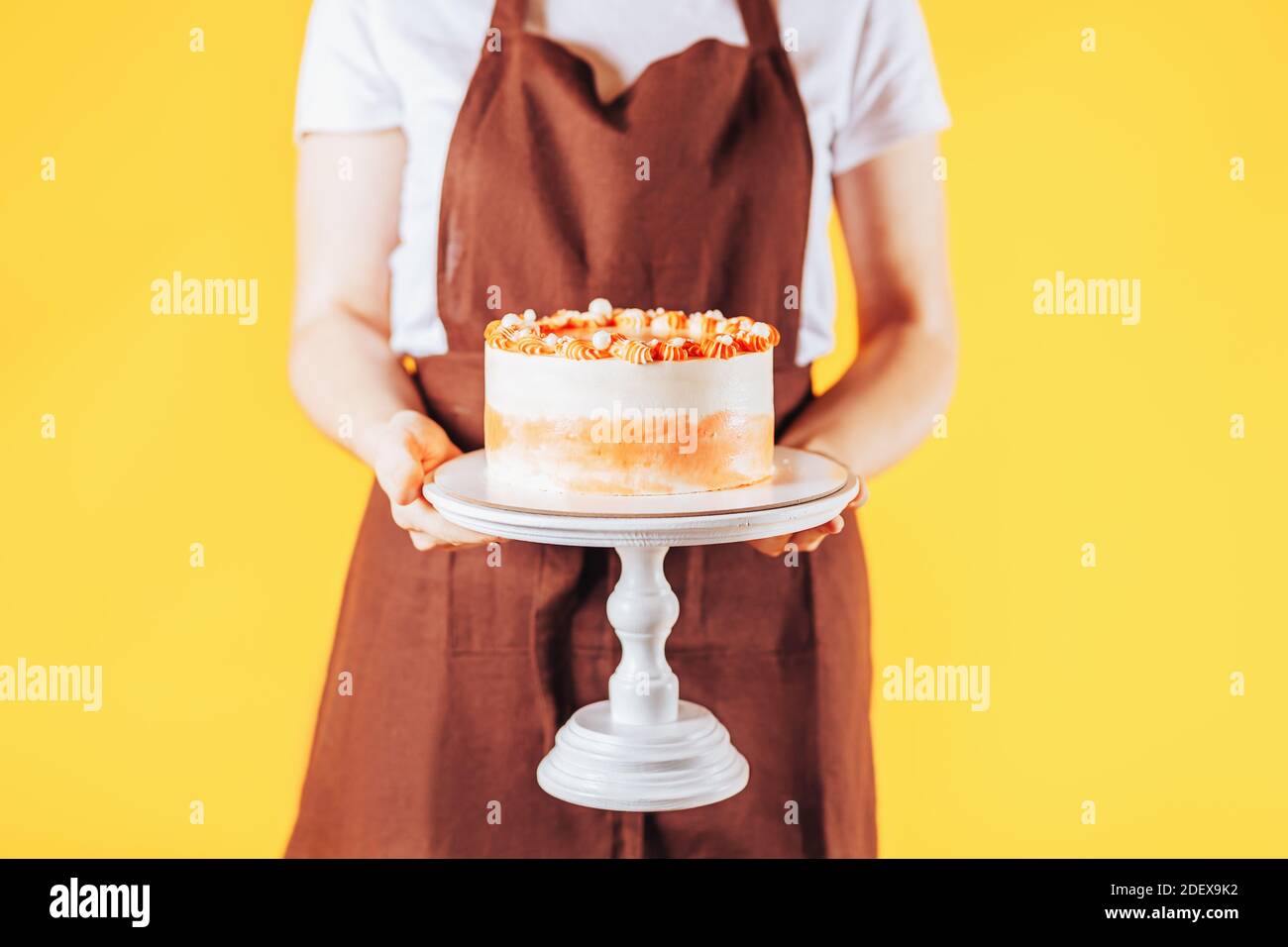 Woman baker holding cake on a stand. Uniforms of kitchen workers in ...