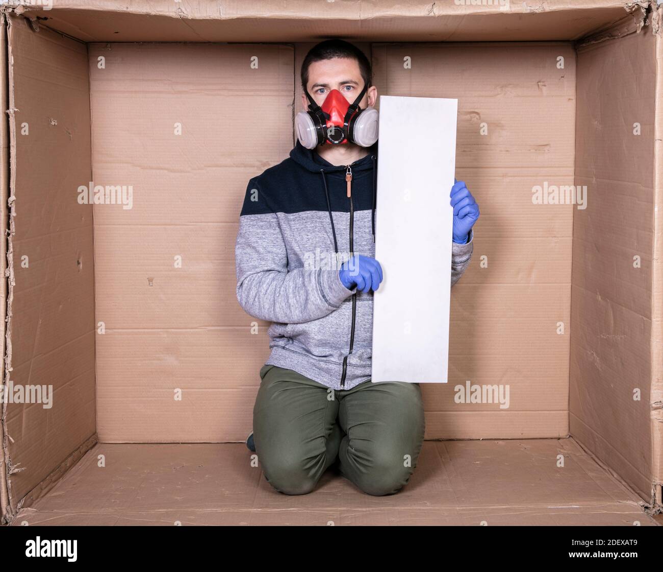 man in a protective mask is sitting in a cardboard box, holding an ...