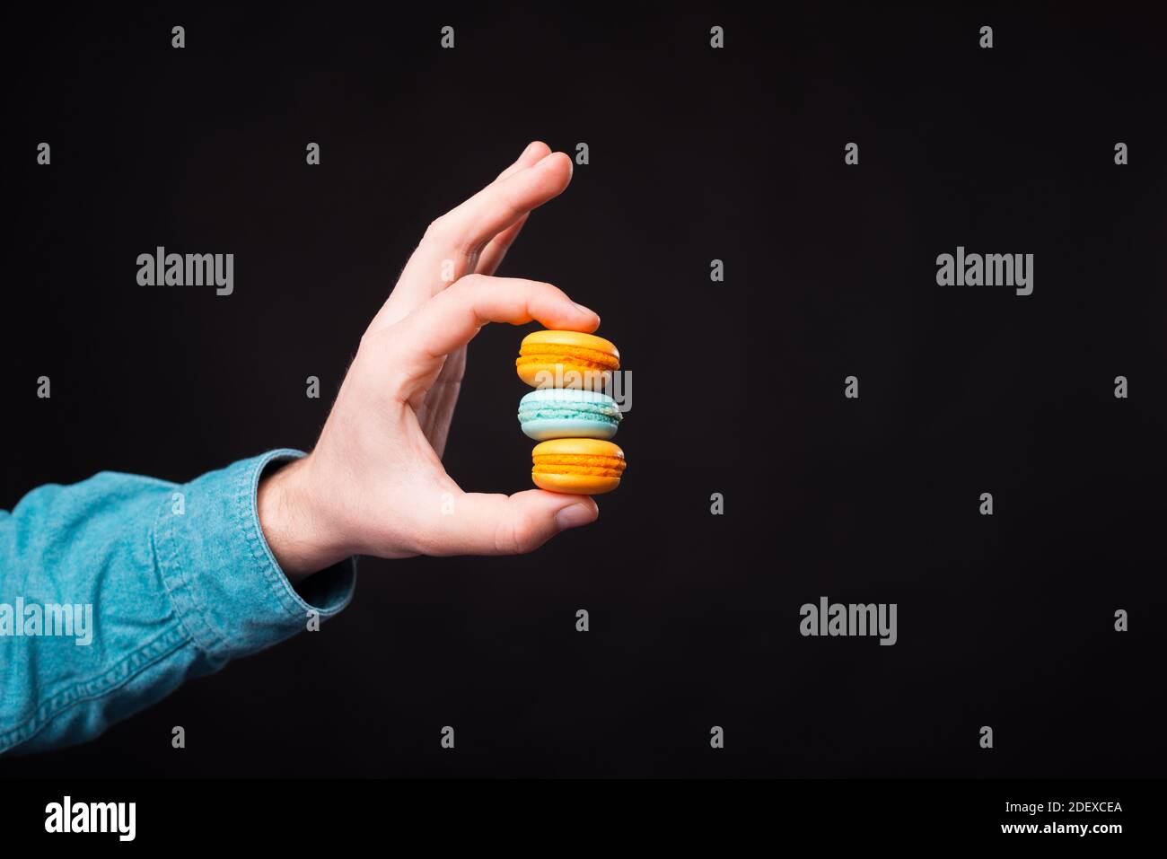 A man is holding three macaroons over black background Stock Photo - Alamy