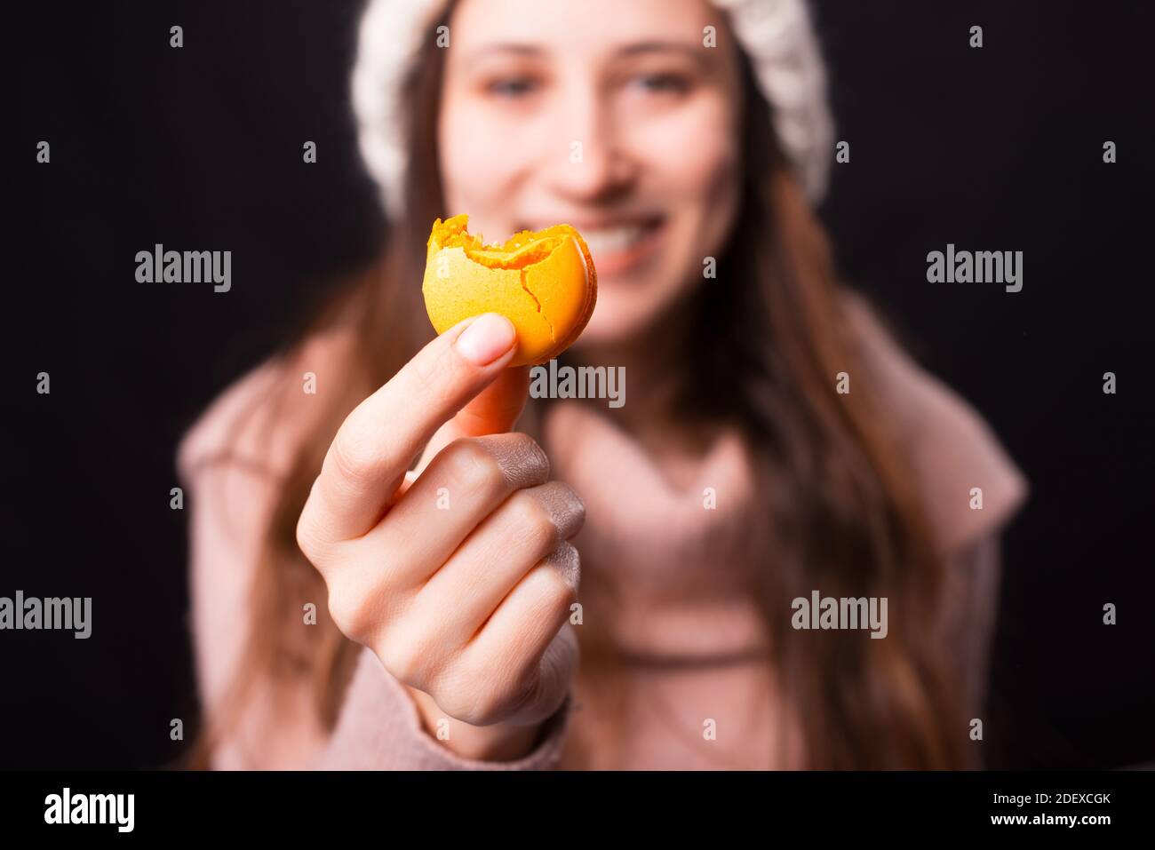 Bitten yellow macaroon is held by a pretty smiling girl over black ...
