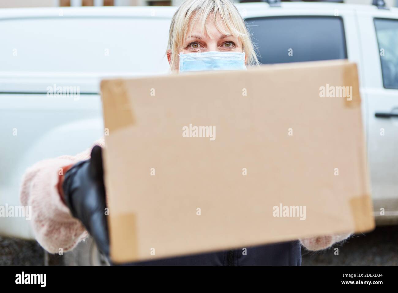 Parcel delivery woman with face mask holds package delivery at camera ...