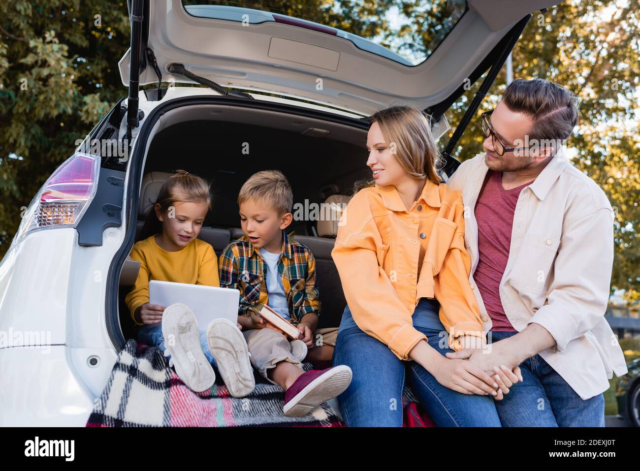 Smiling parents holding hands and looking at kids with book and digital ...