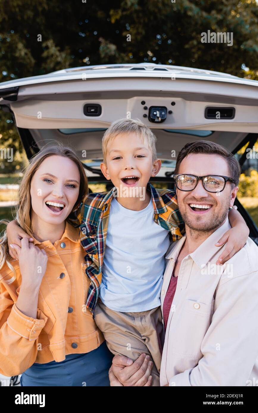 Cheerful boy hugging parents near car during trip outdoors Stock Photo ...