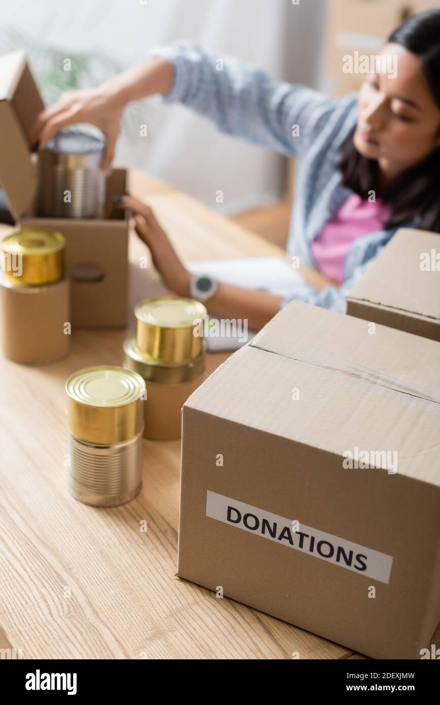 Box with donations lettering near canned food and asian volunteer on ...