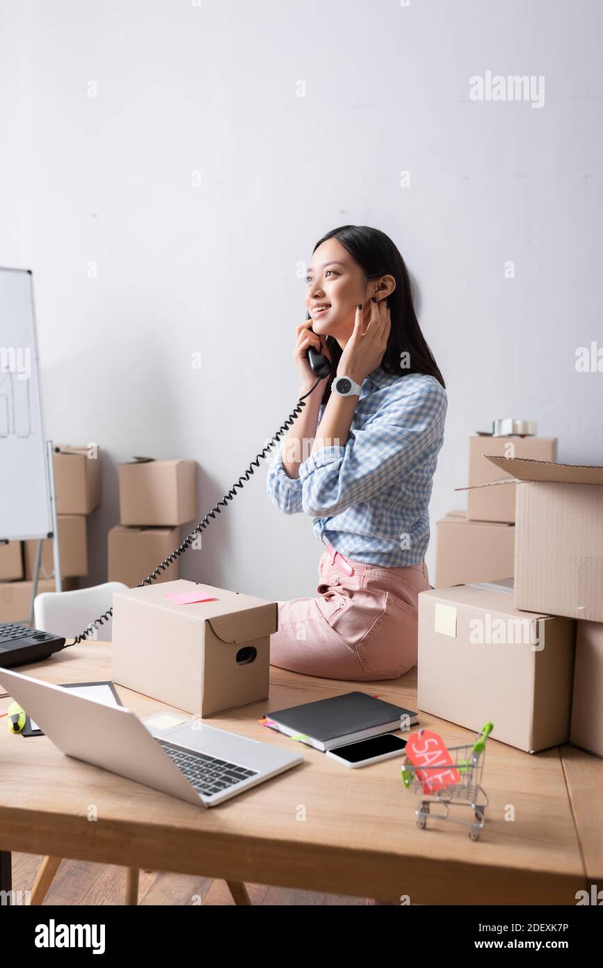 Smiling asian volunteer talking on telephone while sitting on desk with ...