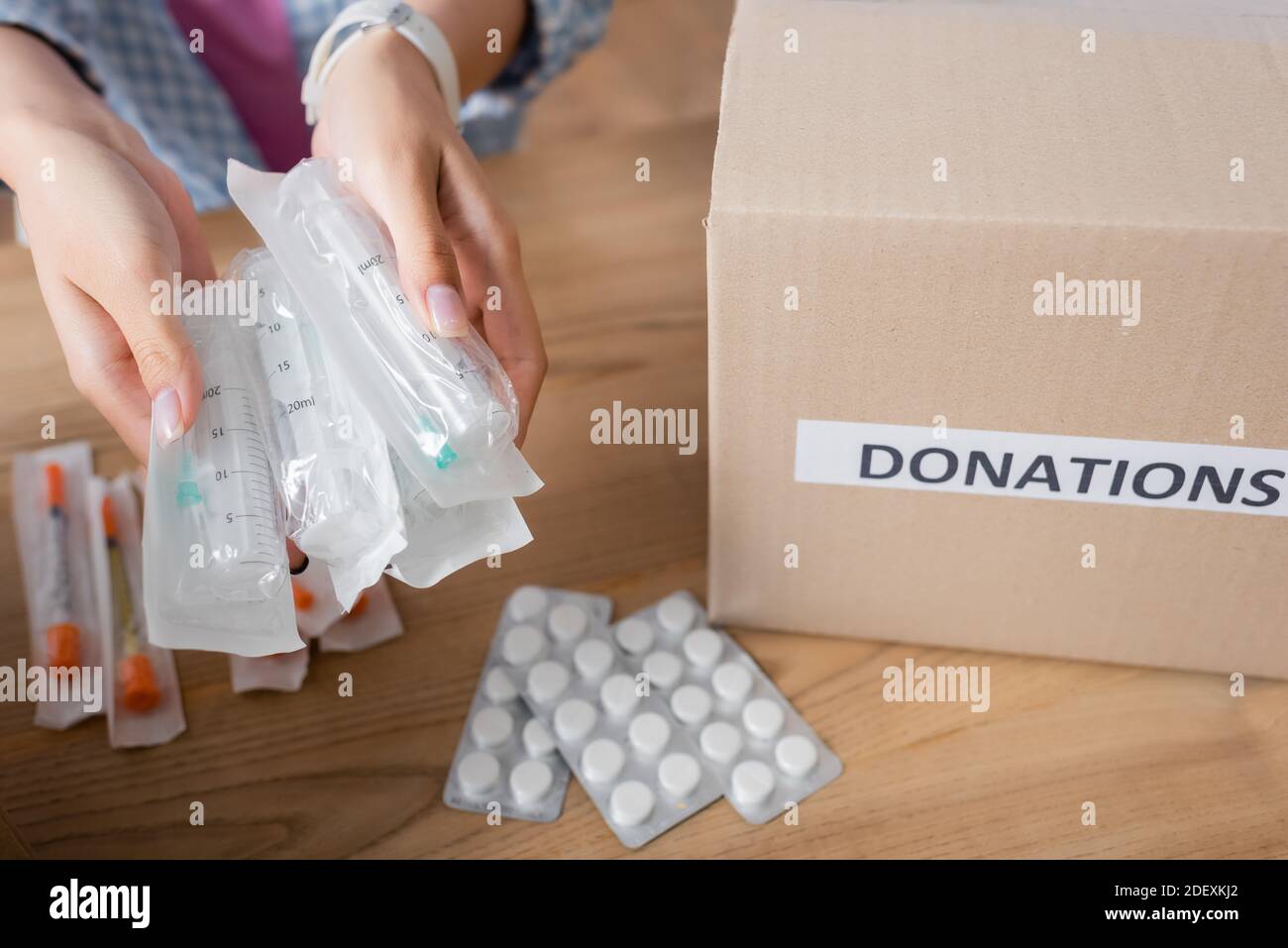 Cropped view of syringes in hands of volunteer near pills and box with ...
