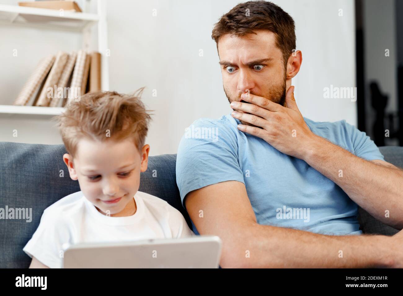 Worried father peeking at what his son is watching on digital tablet ...