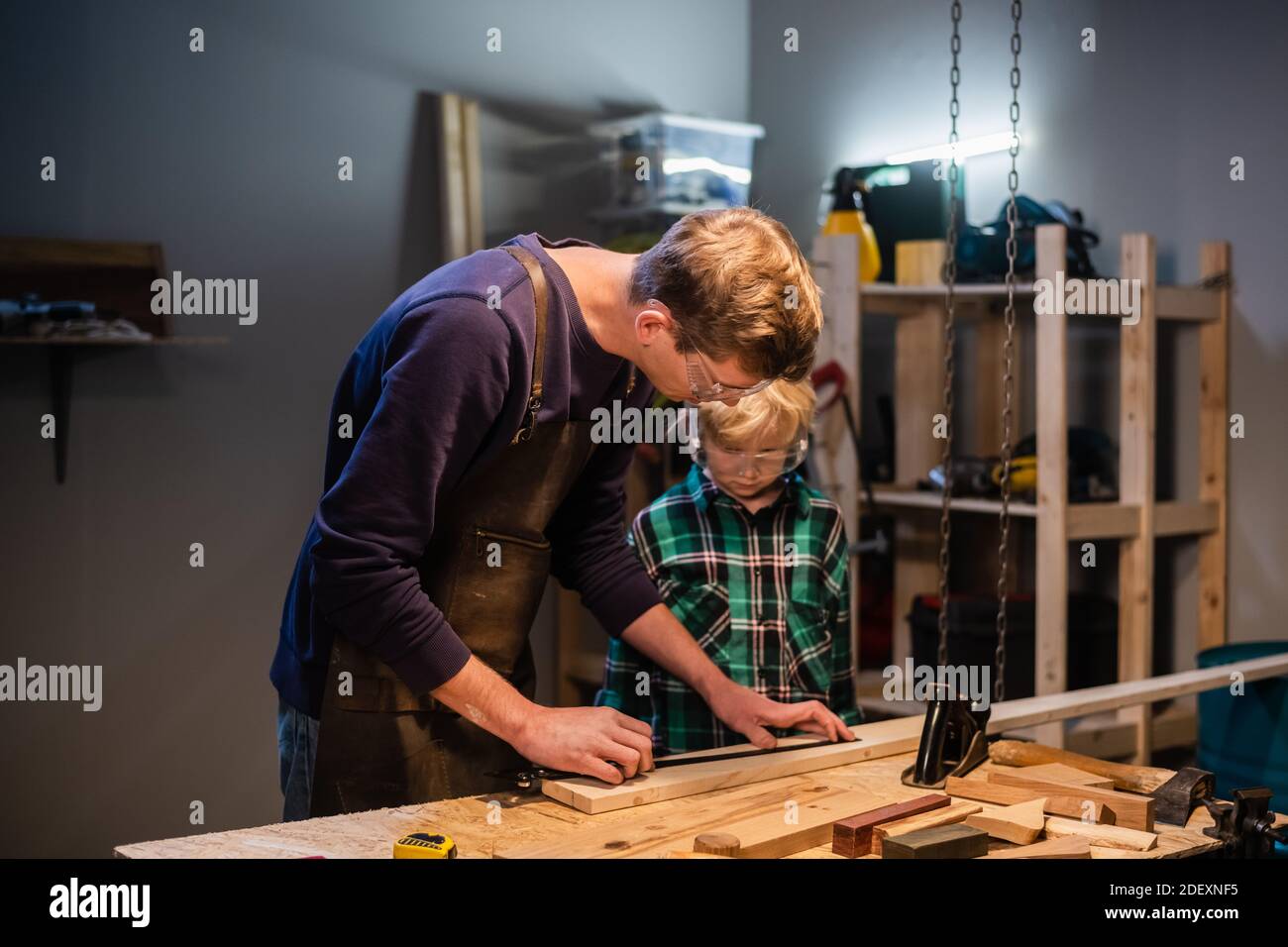 a young male carpenter is teaching woodwork to a young boy in his ...